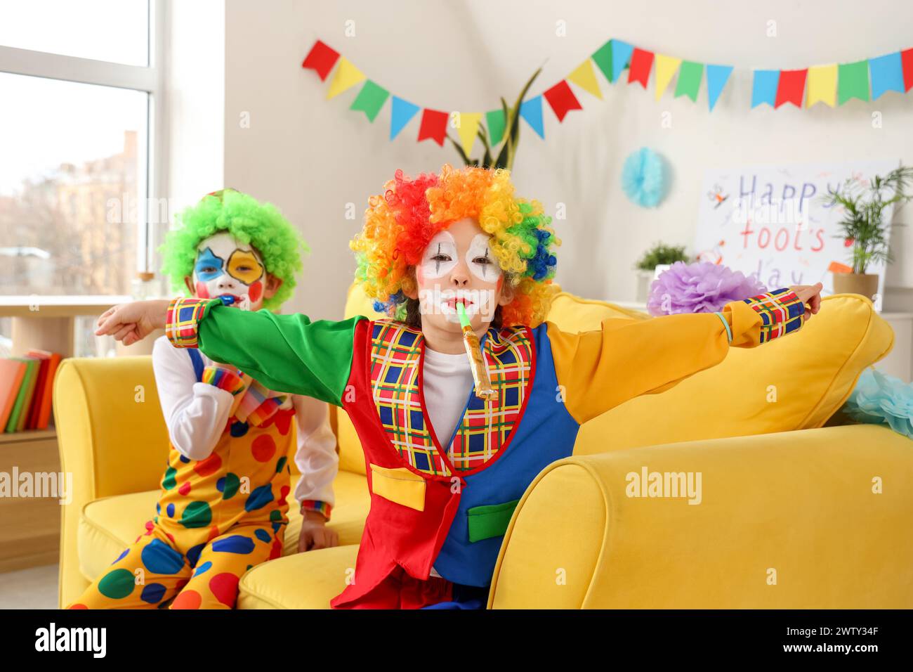 Funny little children in clown costumes with party whistles at home ...