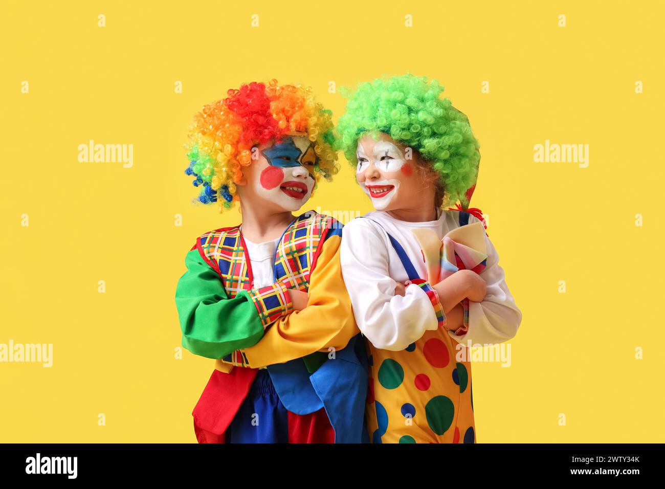 Funny little children in clown costumes on yellow background. April ...