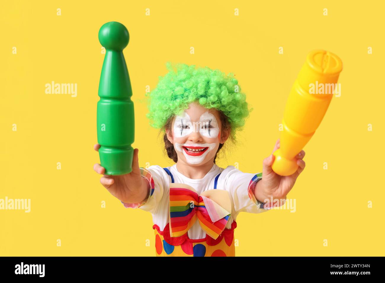 Funny little girl in clown costume with juggling clubs on yellow ...
