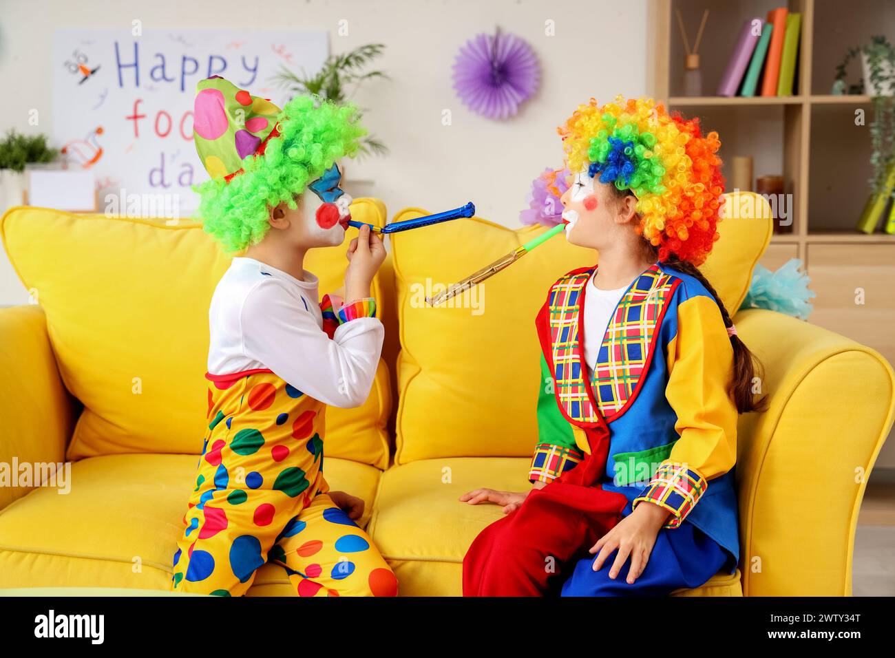Funny little children in clown costumes with party whistles at home ...