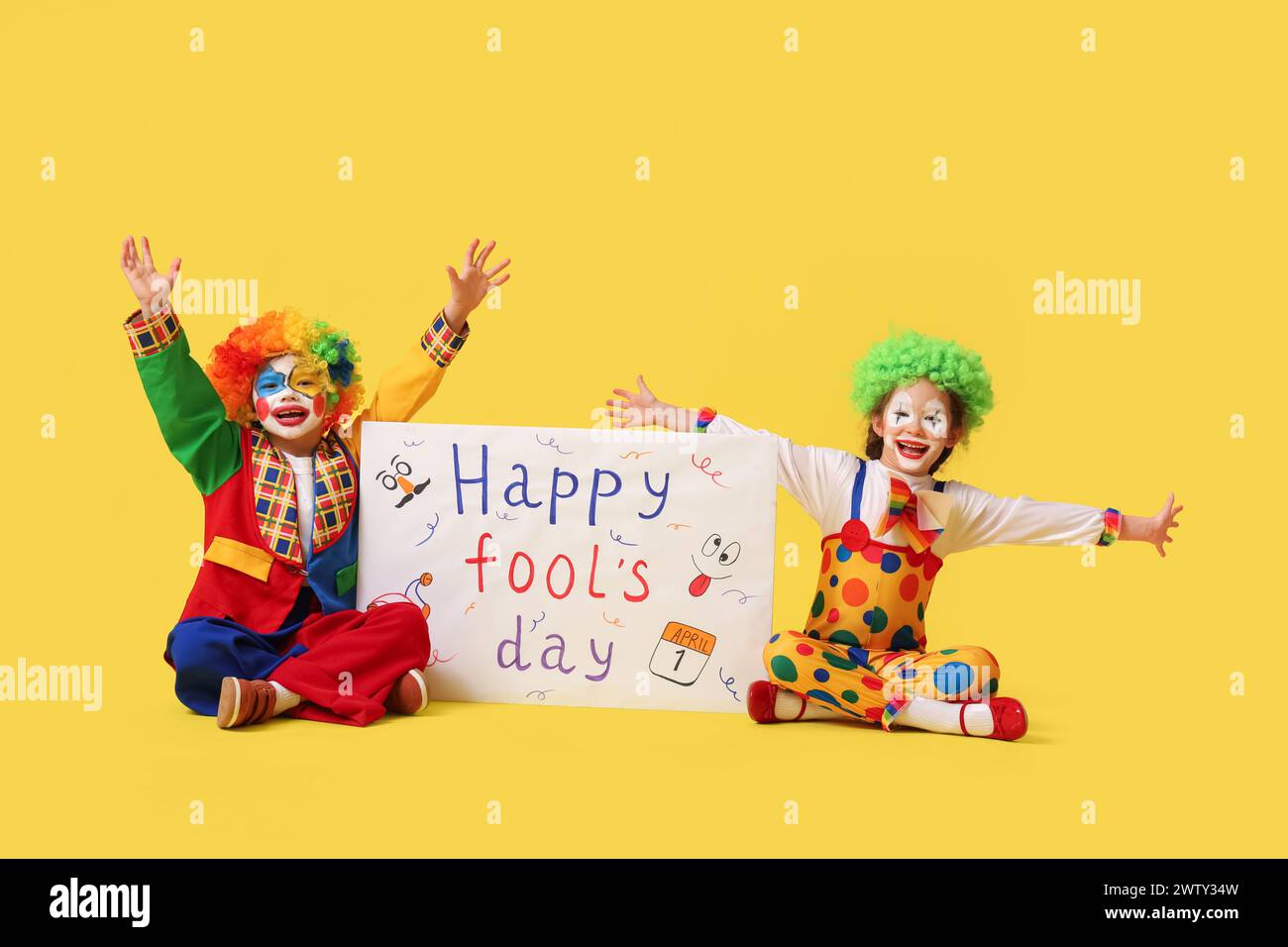 Funny little children in clown costumes with poster sitting on yellow ...