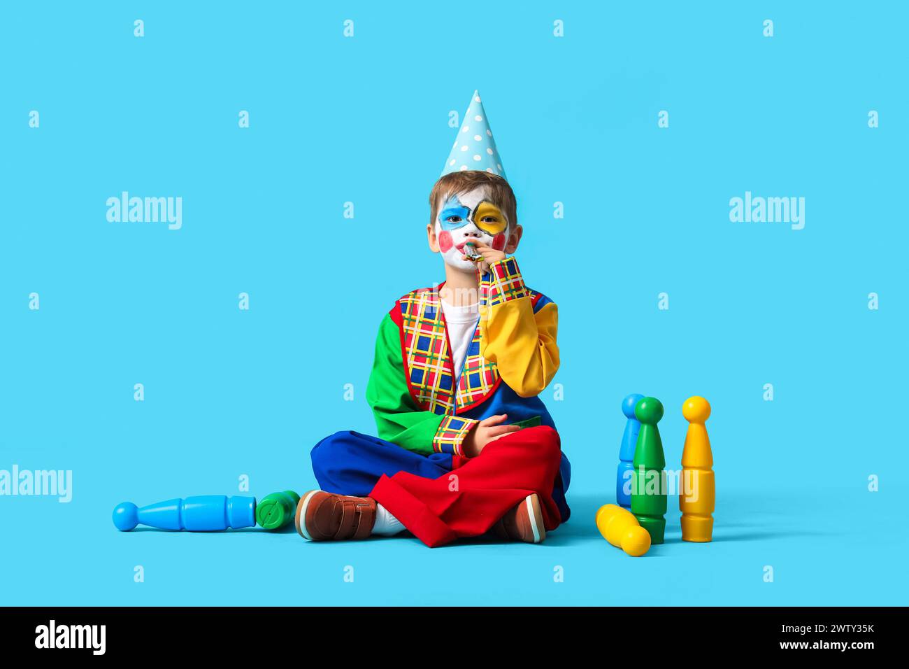 Funny little boy in clown costume with party whistle and juggling clubs ...