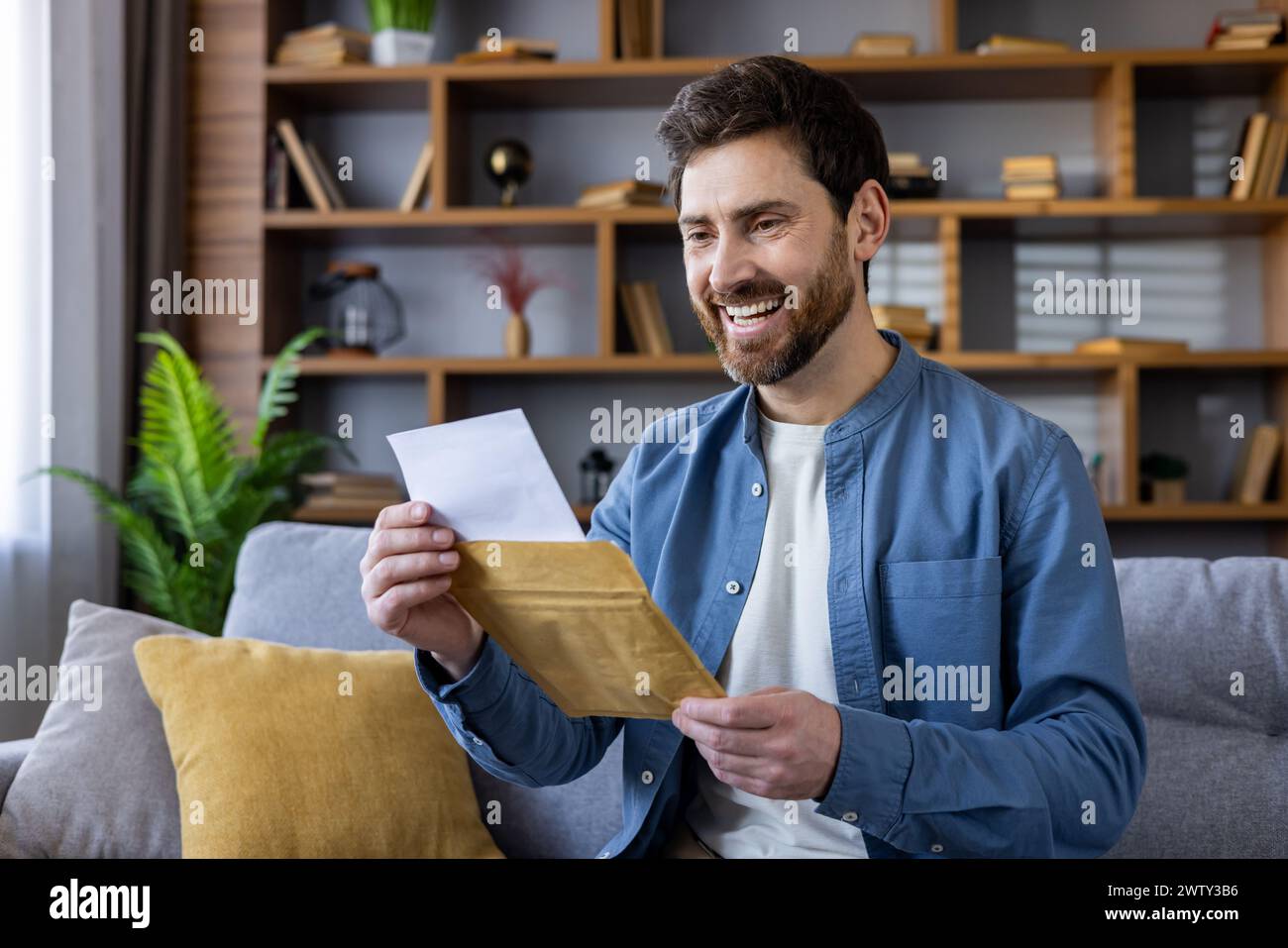 Happy adult male in a casual shirt, enjoying reading a letter while sitting comfortably on a ...