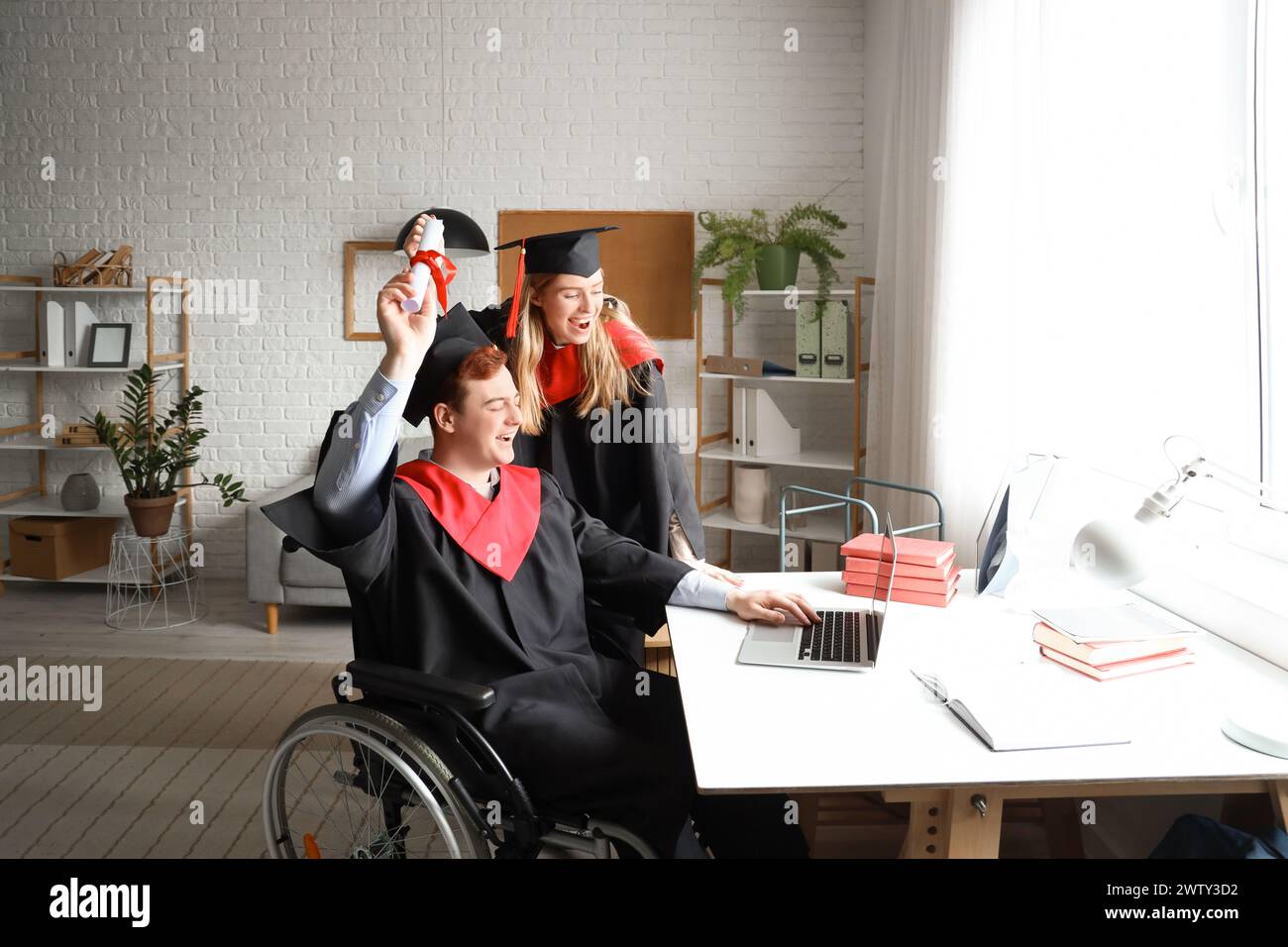 Male graduate in wheelchair with diploma and classmate video chatting ...