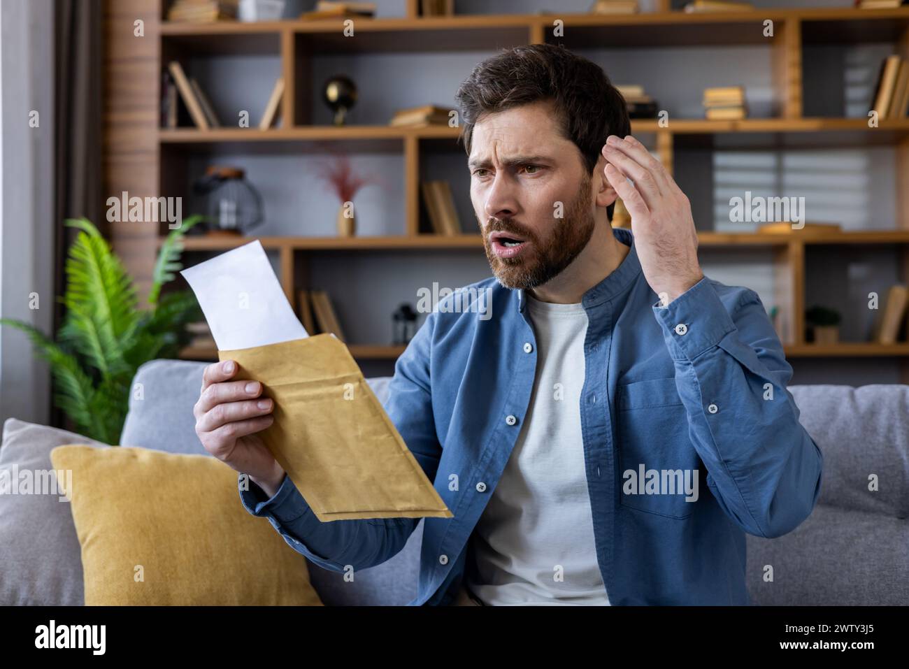 A surprised and concerned man sitting on a couch, holding and looking ...