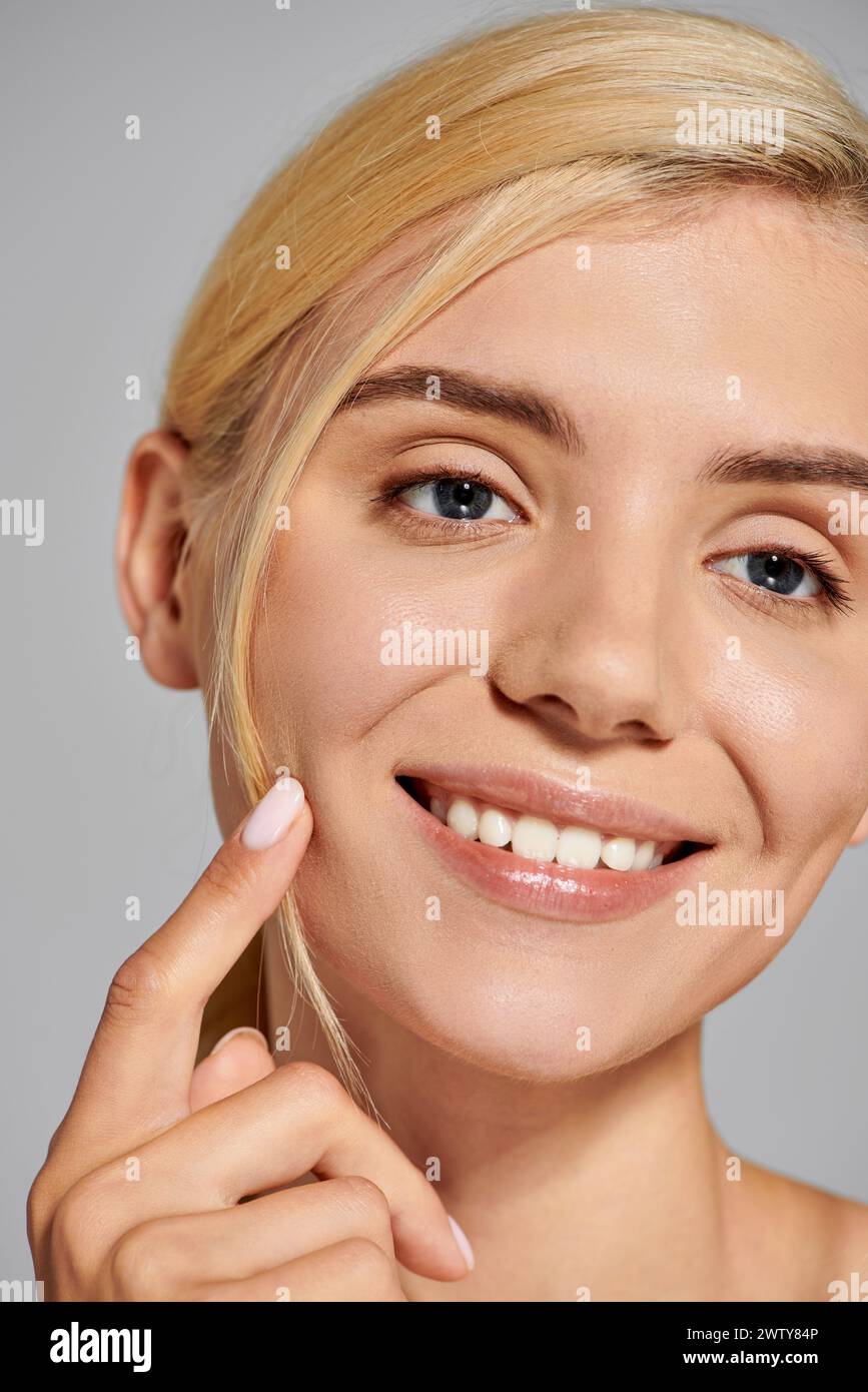 charming woman face with clear skin smiles and touches skin with ...