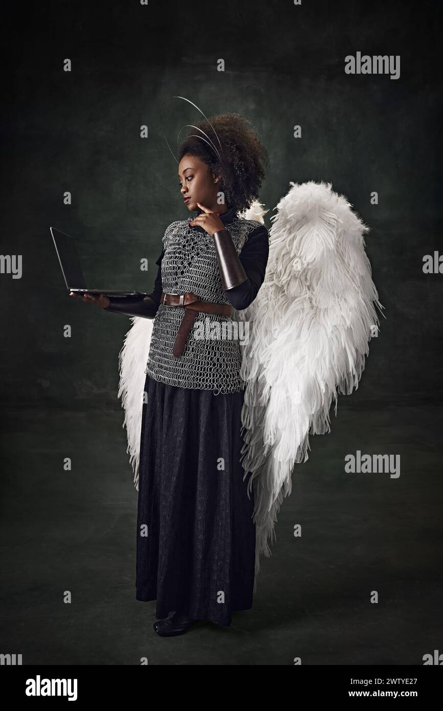 Young African woman, medieval warrior with angel wings holding laptop ...