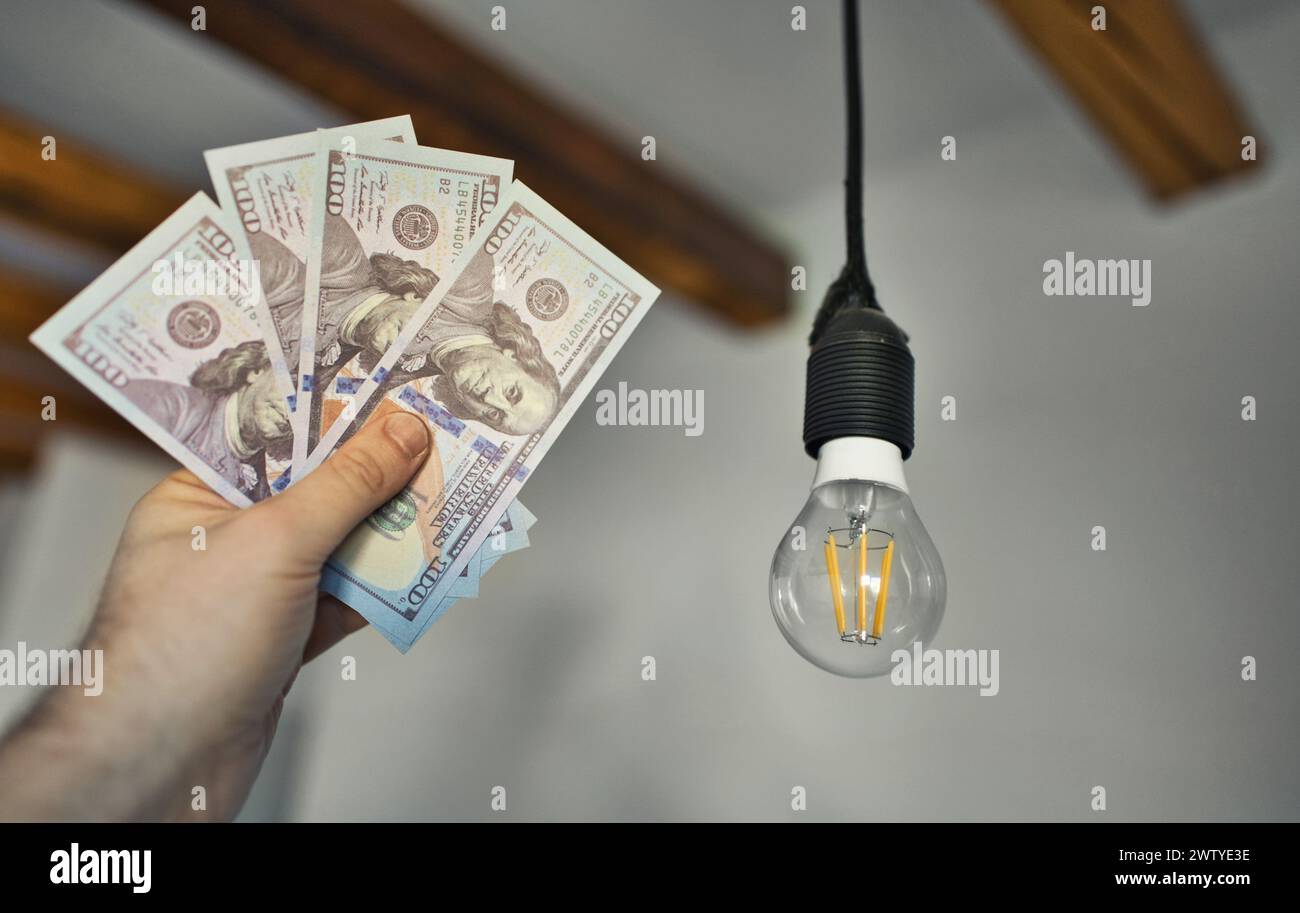 Man holds money next to a light bulb. Expensive electricity concept ...