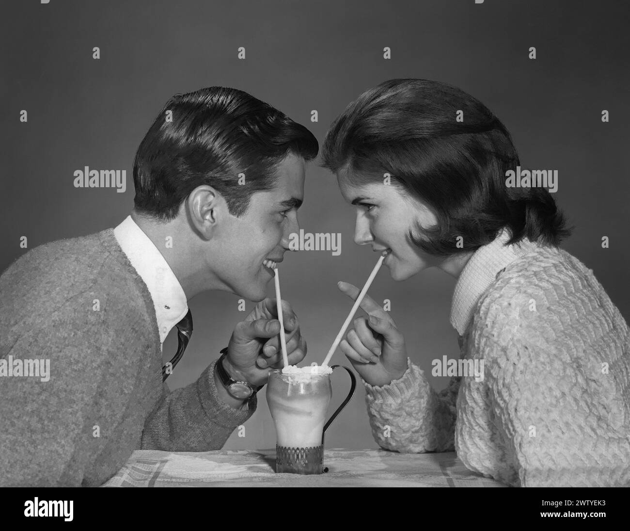 Smartly dressed young couple facing each other share a milkshake Stock ...