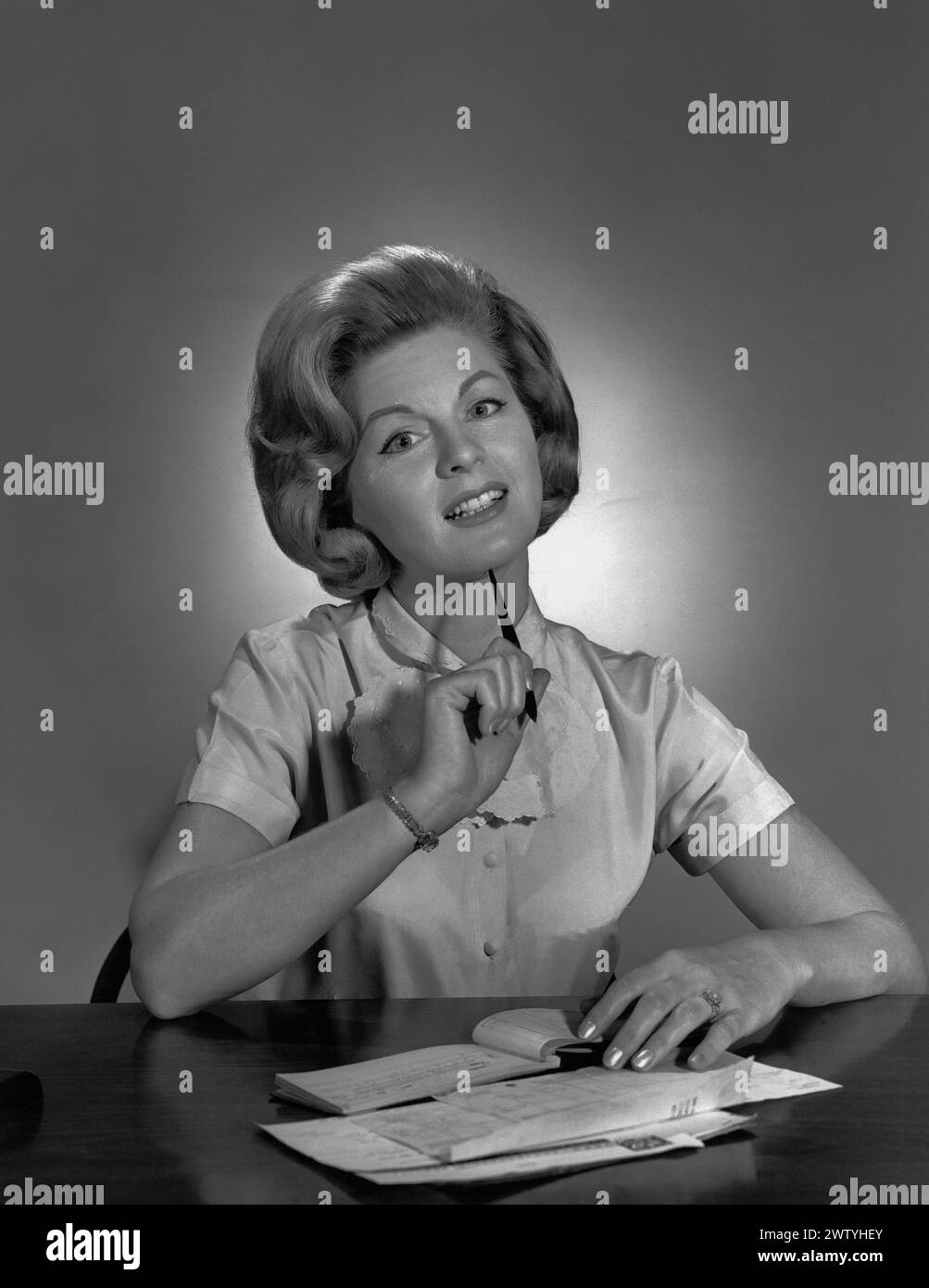 Woman in a short sleeve dress sitting at a table ponders the stack of ...