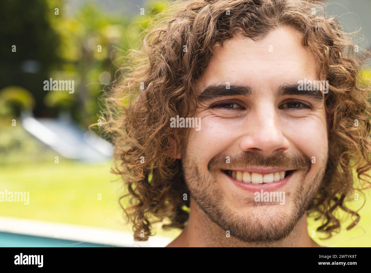 A young Caucasian man smiles broadly outdoors, showcasing curly brown ...