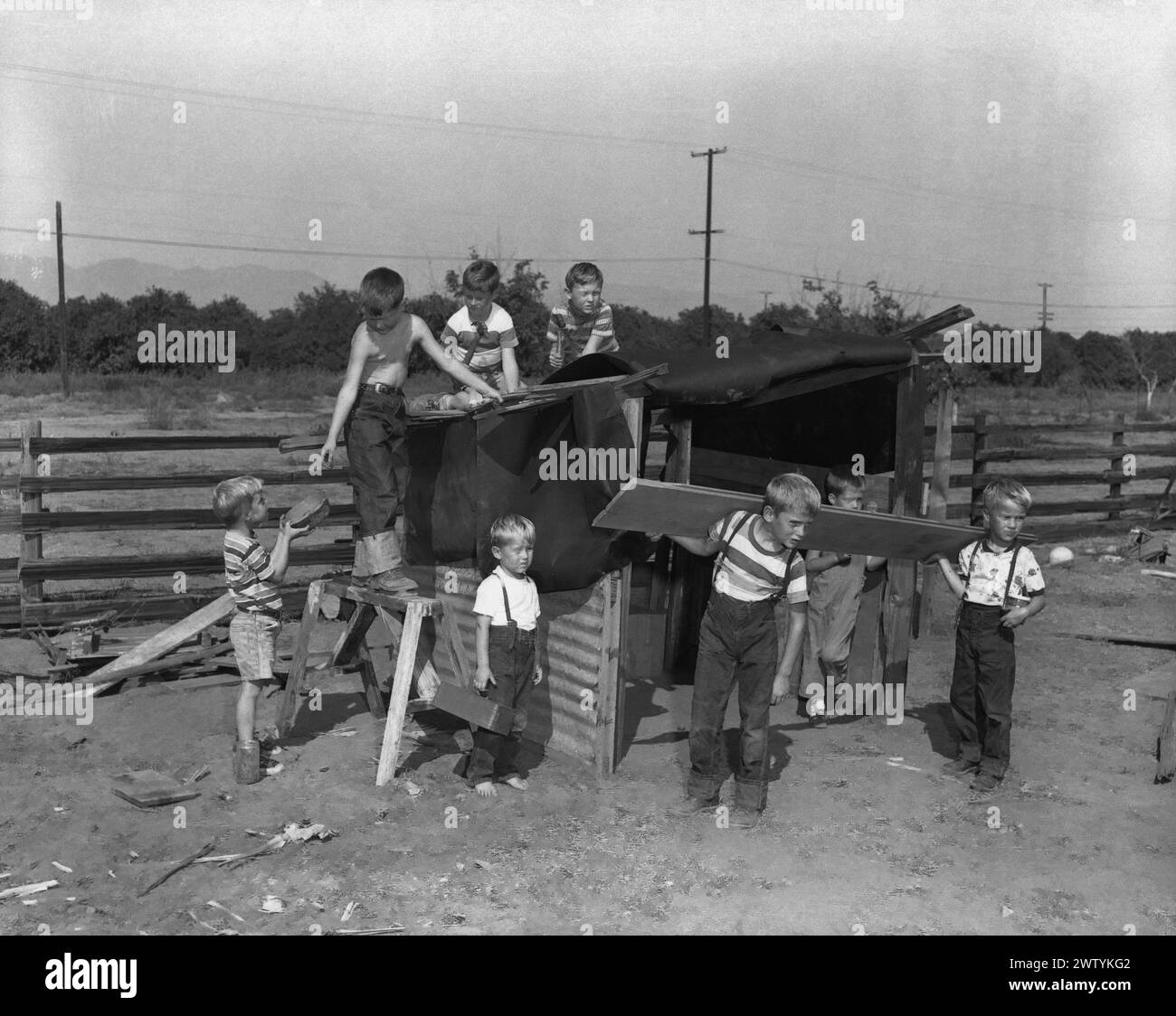 Group of young boys outside building a hut on the roof two can be seen ...