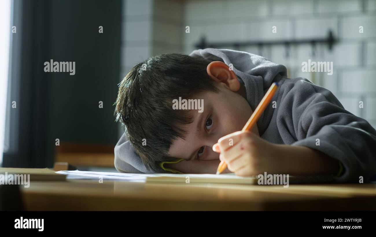 Tired schoolboy kid lying on table desk writing homework, boring class ...