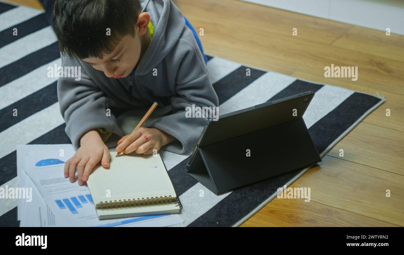 Cute kid lying on the floor studying with tablet computer writing in ...