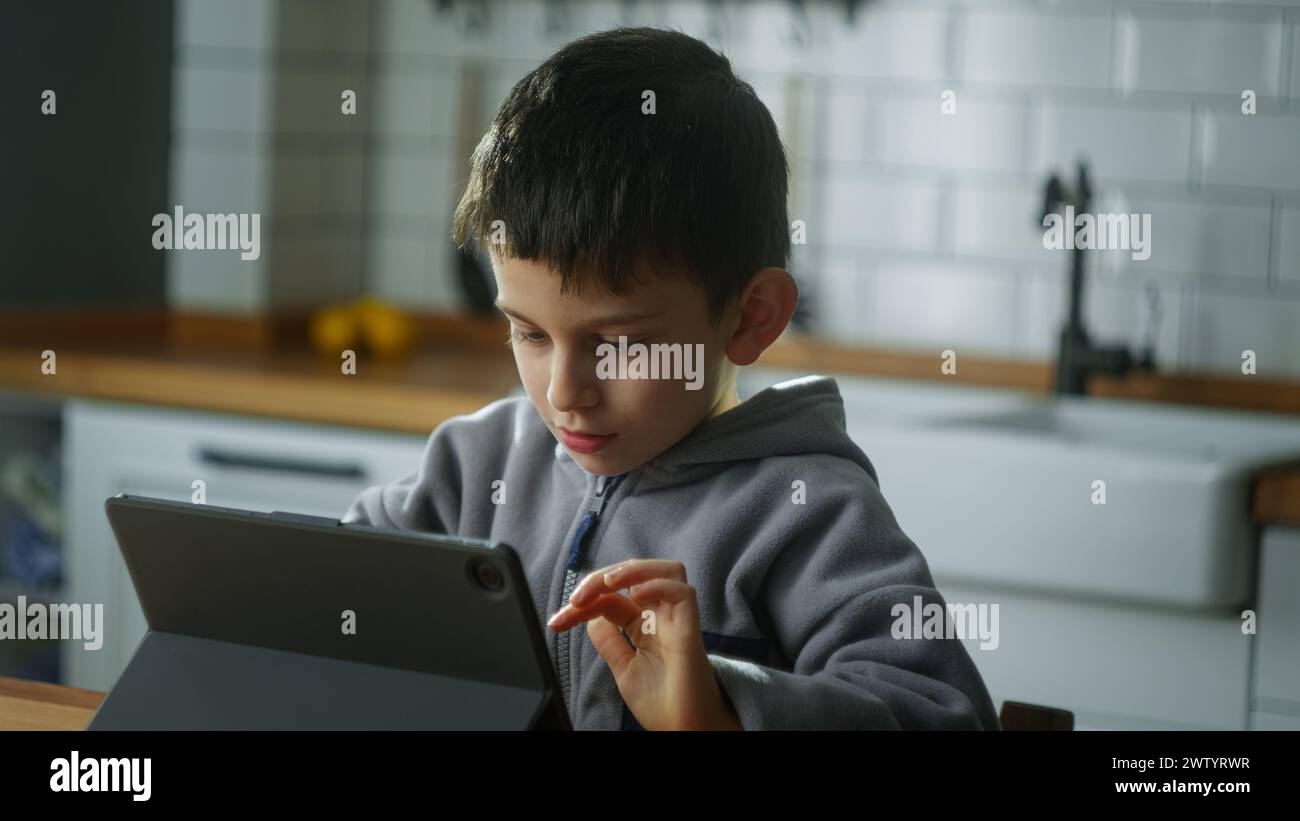 Cute little boy sitting in the kitchen playing mobile game on digital ...