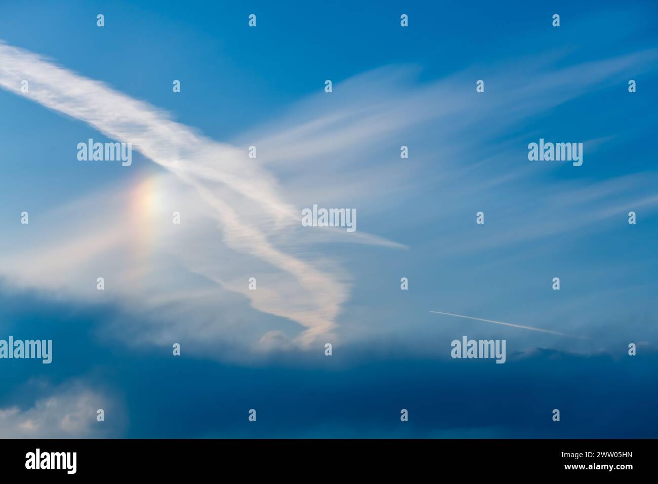 Sky with cirrus, stratus clouds, airplane trail and halo from the sun ...