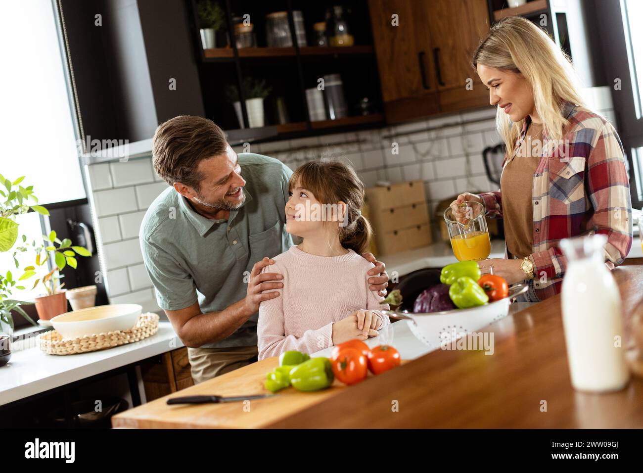 Young family chatting and preparing food around a bustling kitchen ...