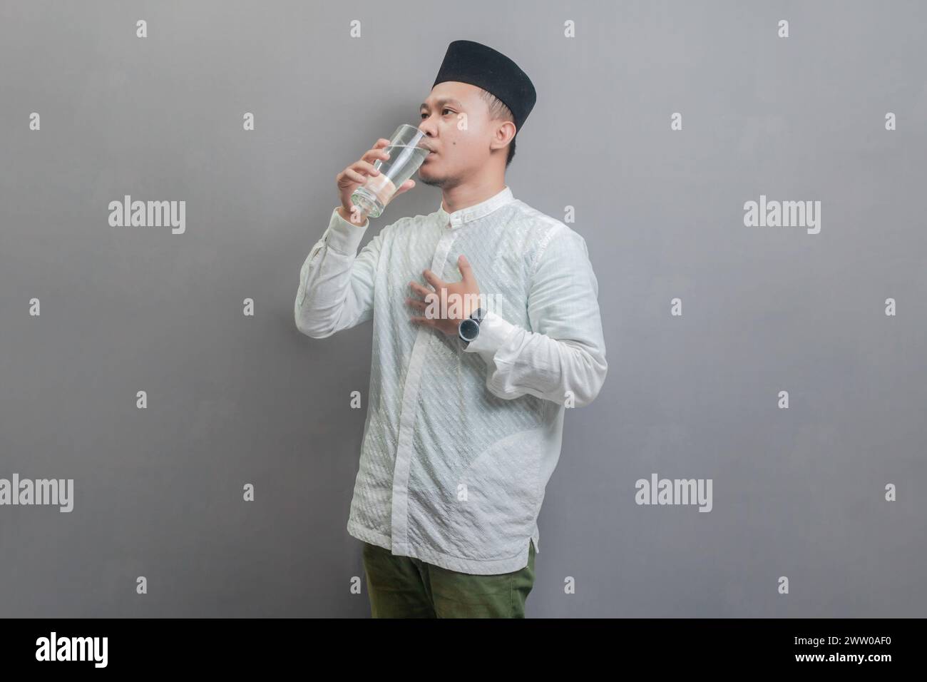 Happy asian muslim man drinking a fresh glass of pure water wearing a ...