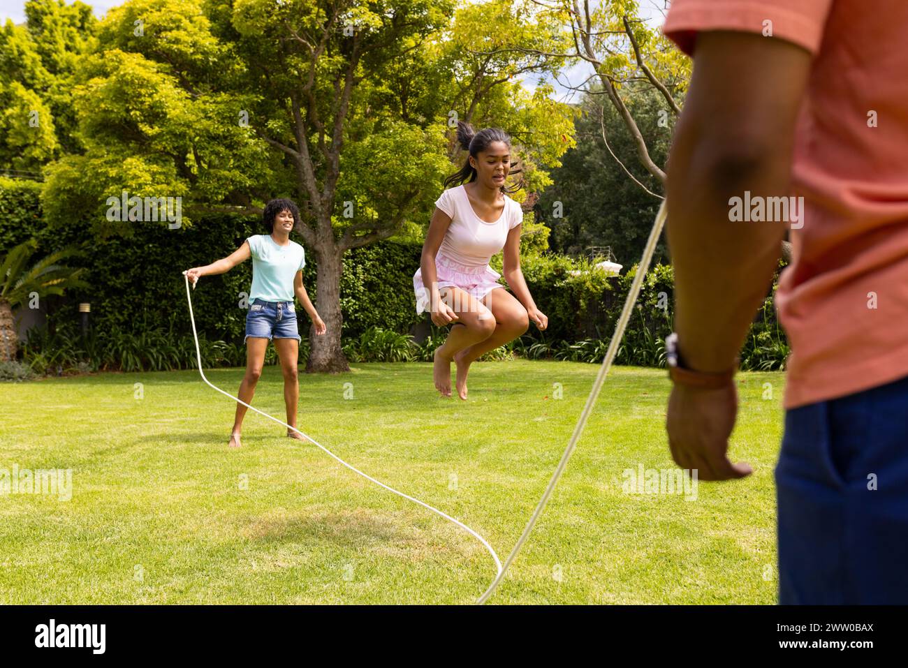 A family enjoys a sunny day with a jump rope activity in the garden ...