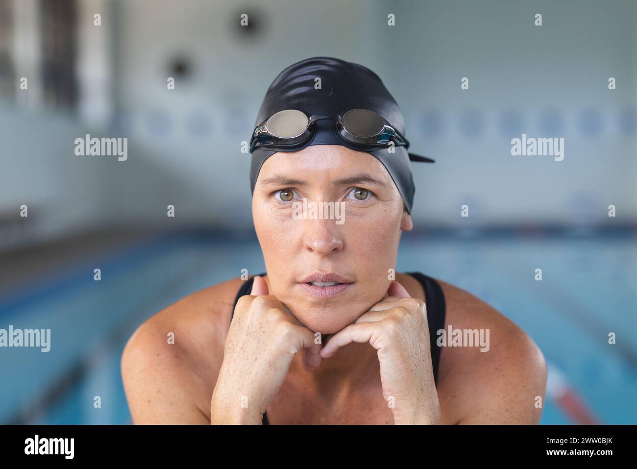 A middle-aged Caucasian female athlete swimmer rests at the pool's edge ...
