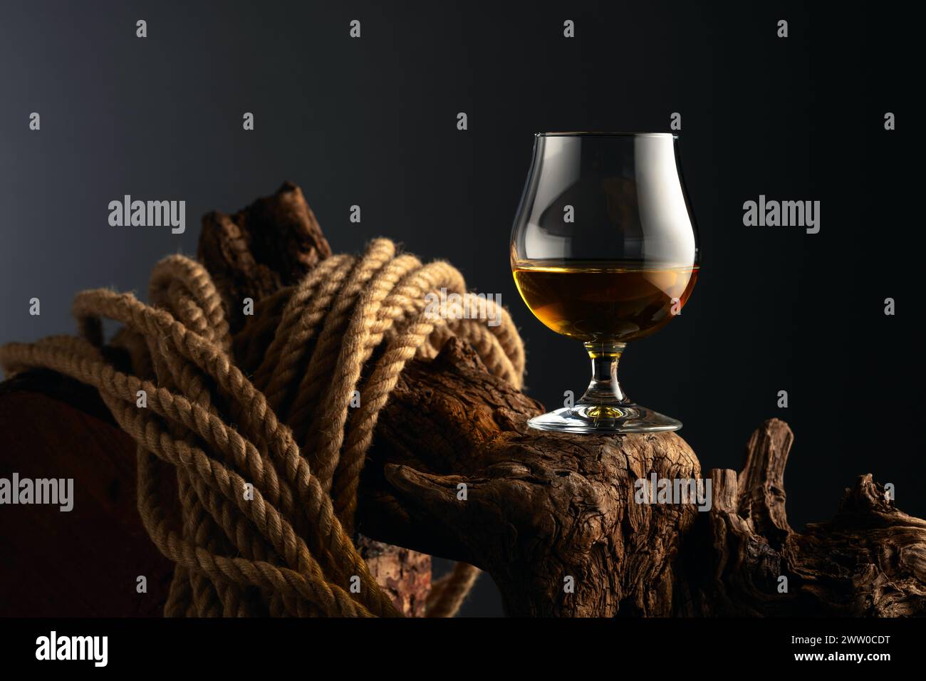 Brandy snifter and rope on a old wooden snag. Glass with whiskey ...