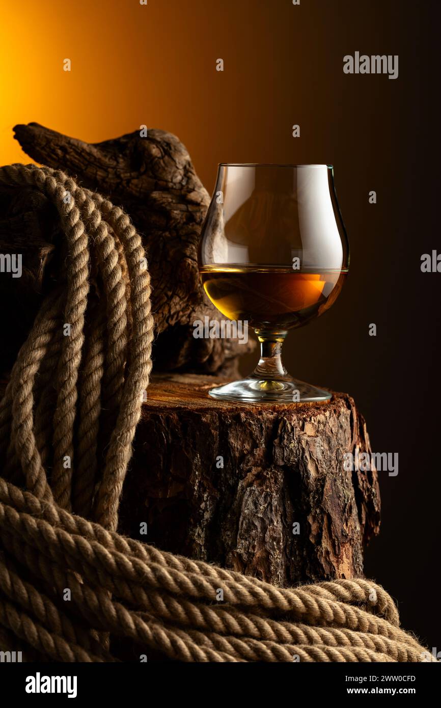 Brandy snifter and rope on a old stumb. Glass with whiskey, cognac or ...