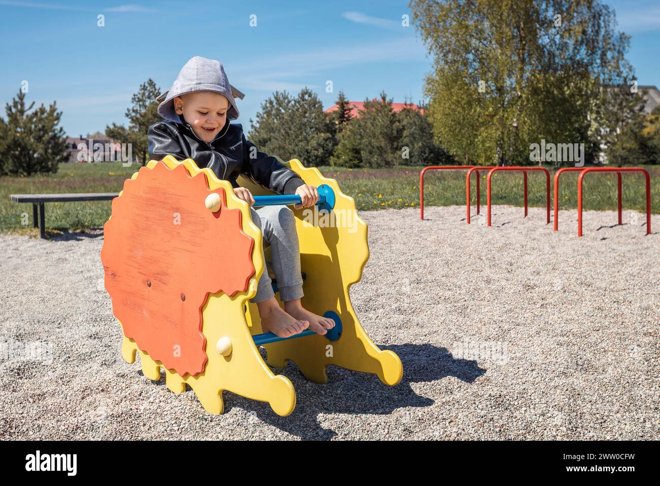 A cute little smiling boy with his baby teeth falling out swings on a spring-loaded hedgehog ...