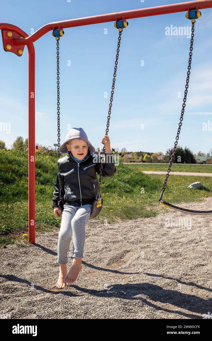 A small, barefoot, toothless boy in a black leather jacket sits on a ...