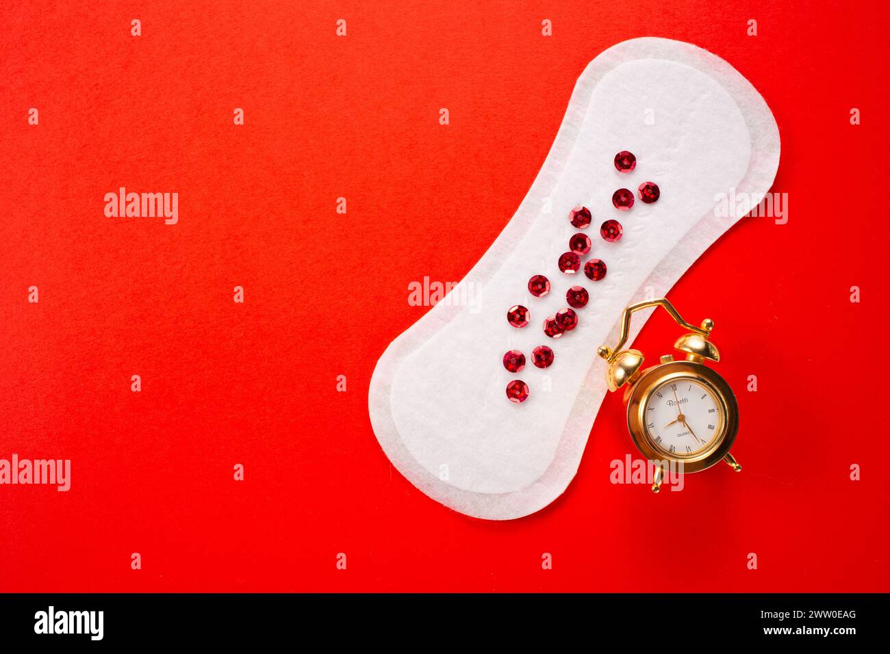 Alarm clock and feminine hygiene pad with red glitter on red background ...