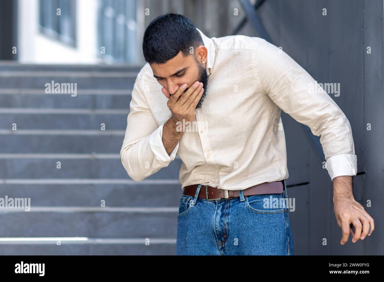 A young Indian man stands outside an office building and covers his ...