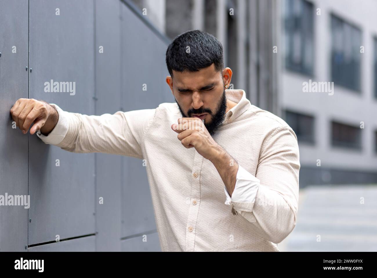 Cough attack. A young Indian man is standing outside the building ...