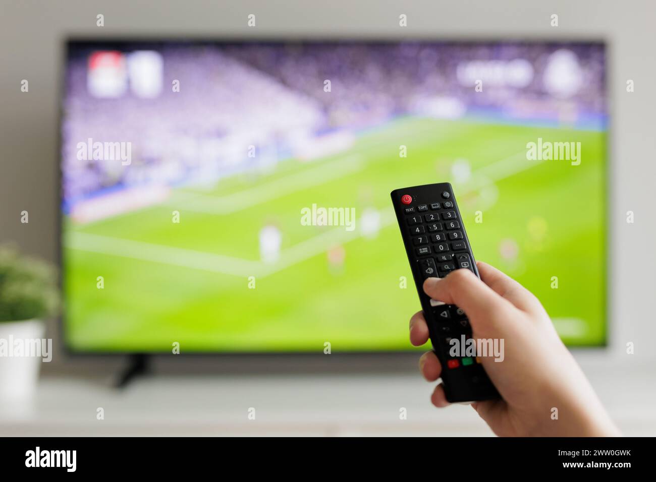 Close up of hand with remote controller and tv with football on ...