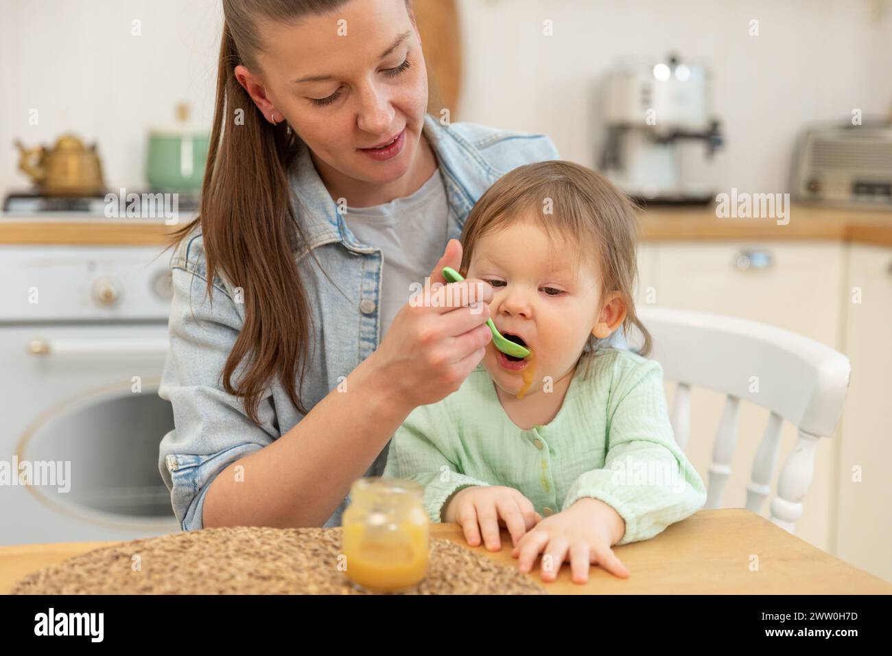 Happy family at home. Mother feeding her baby girl from spoon in ...