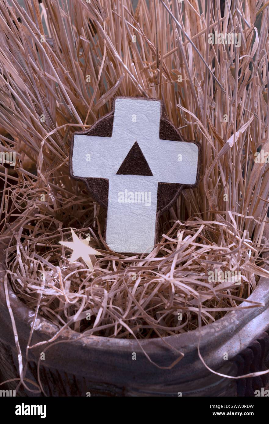 Handcrafted leather cross with triune God symbol rests in a manger bed ...