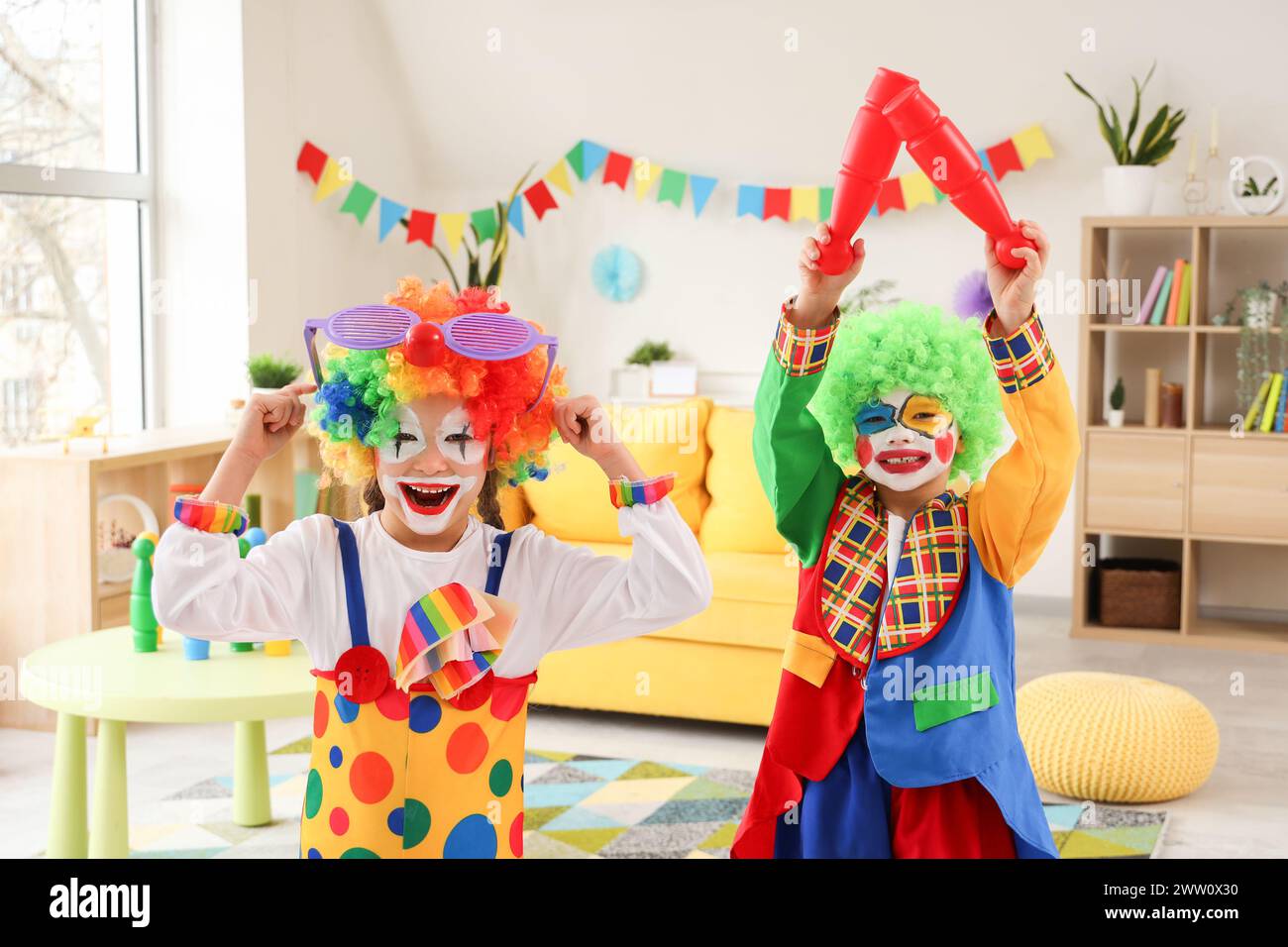 Funny little children in clown costumes with juggling clubs at home ...