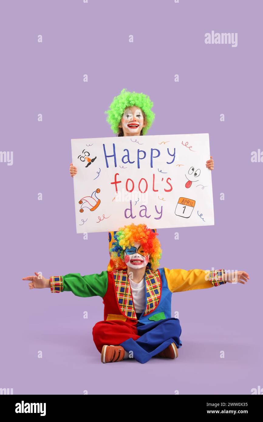 Funny little children in clown costumes with poster on lilac background ...