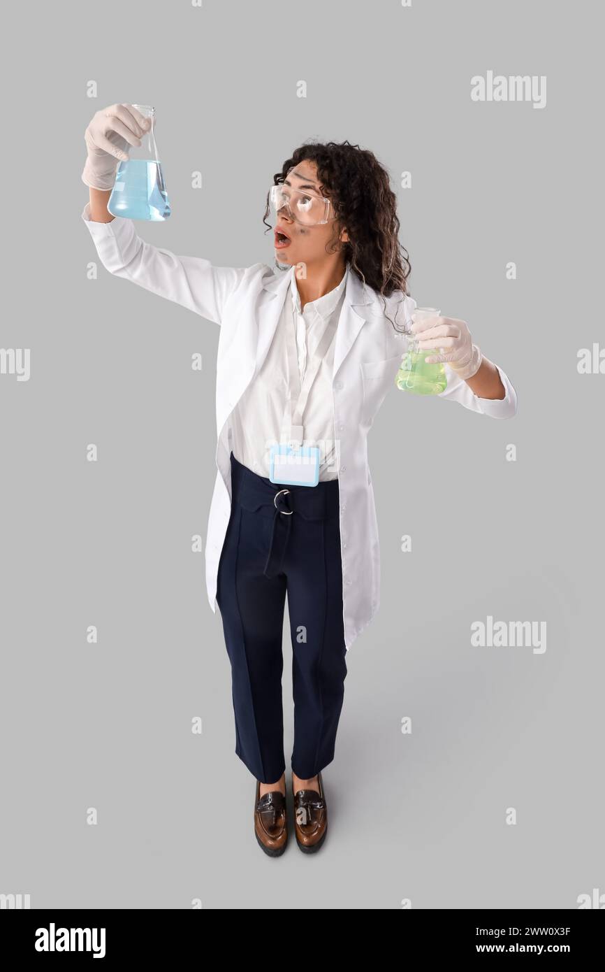 Shocked female African-American chemist with flasks on light background ...