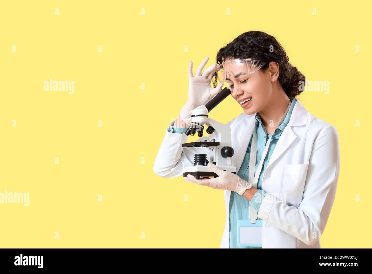 Female African-American chemist with microscope on yellow background ...