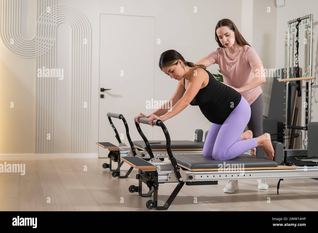 A pregnant woman works out on a reformer exercise machine with a ...