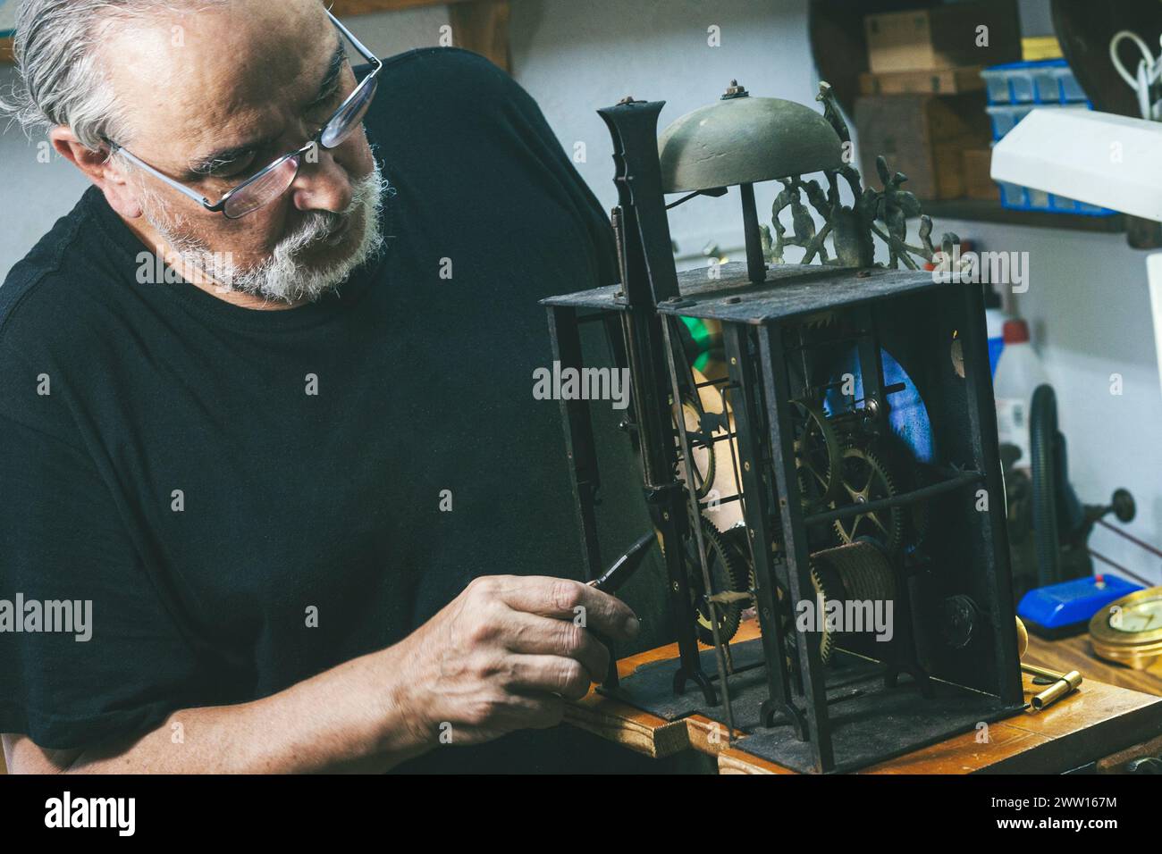 Watchmaker making adjustments to the gears of a large wall clock in his ...
