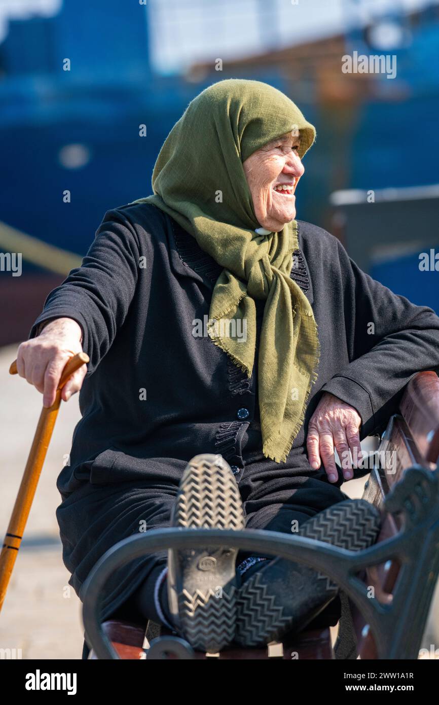 An elderly muslim lady with a walking stick watches the world go by ...