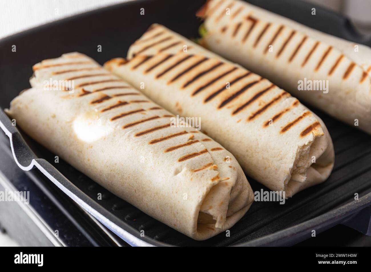 Three wraps with grill marks in a pan, filled shawarma at grill pan ...
