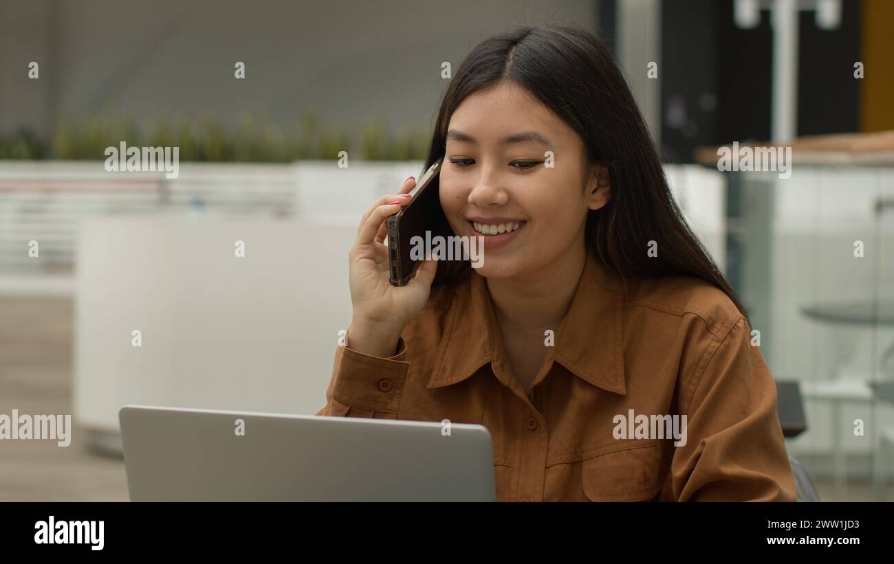 Asian businesswoman work multitask use laptop talk mobile phone solve online project with client ...