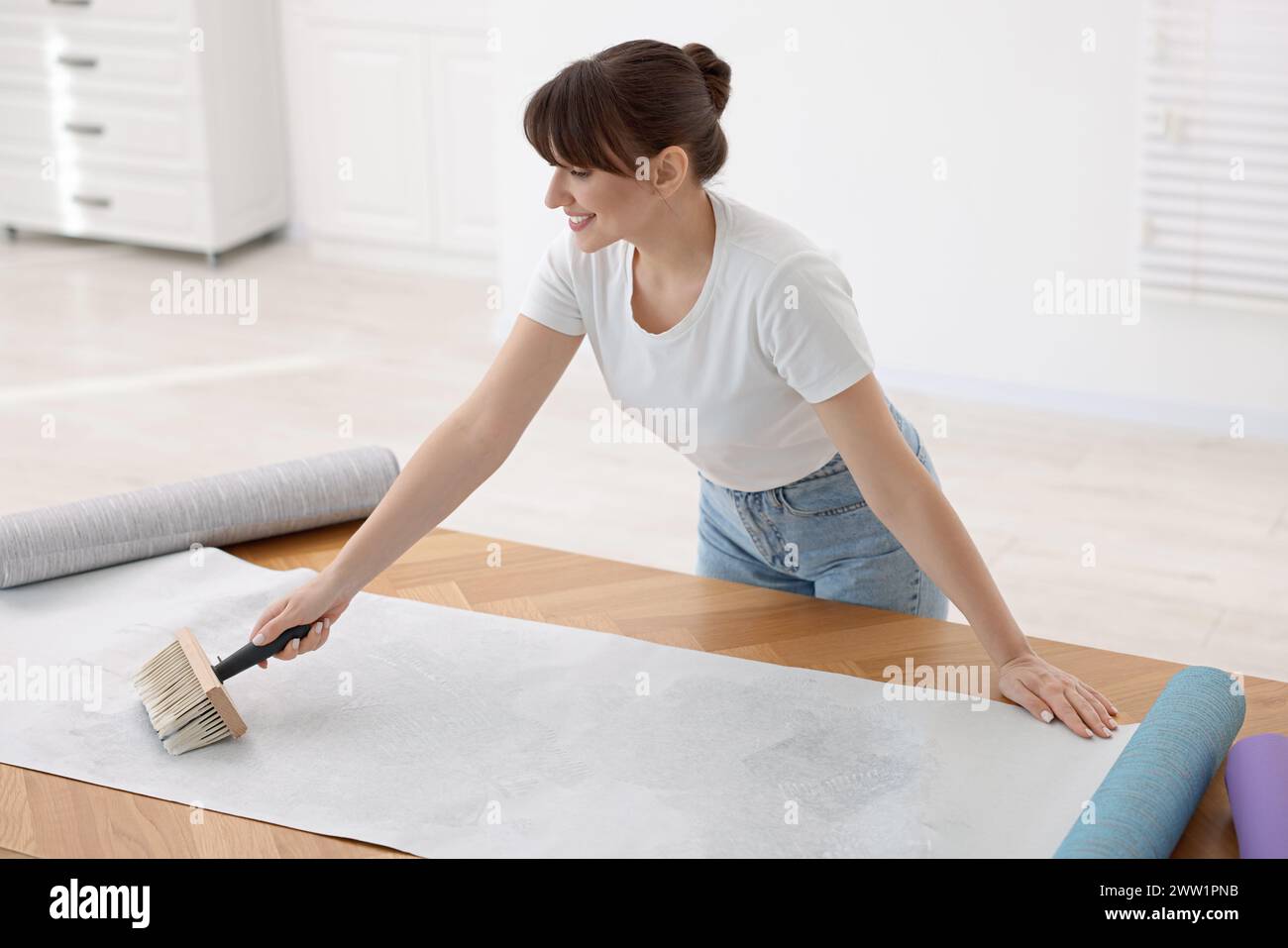 Woman applying glue onto wallpaper sheet at wooden table indoors Stock ...