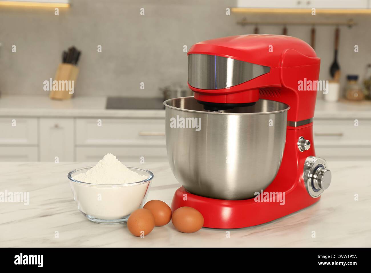 Modern red stand mixer, eggs and bowl with flour on white marble table ...