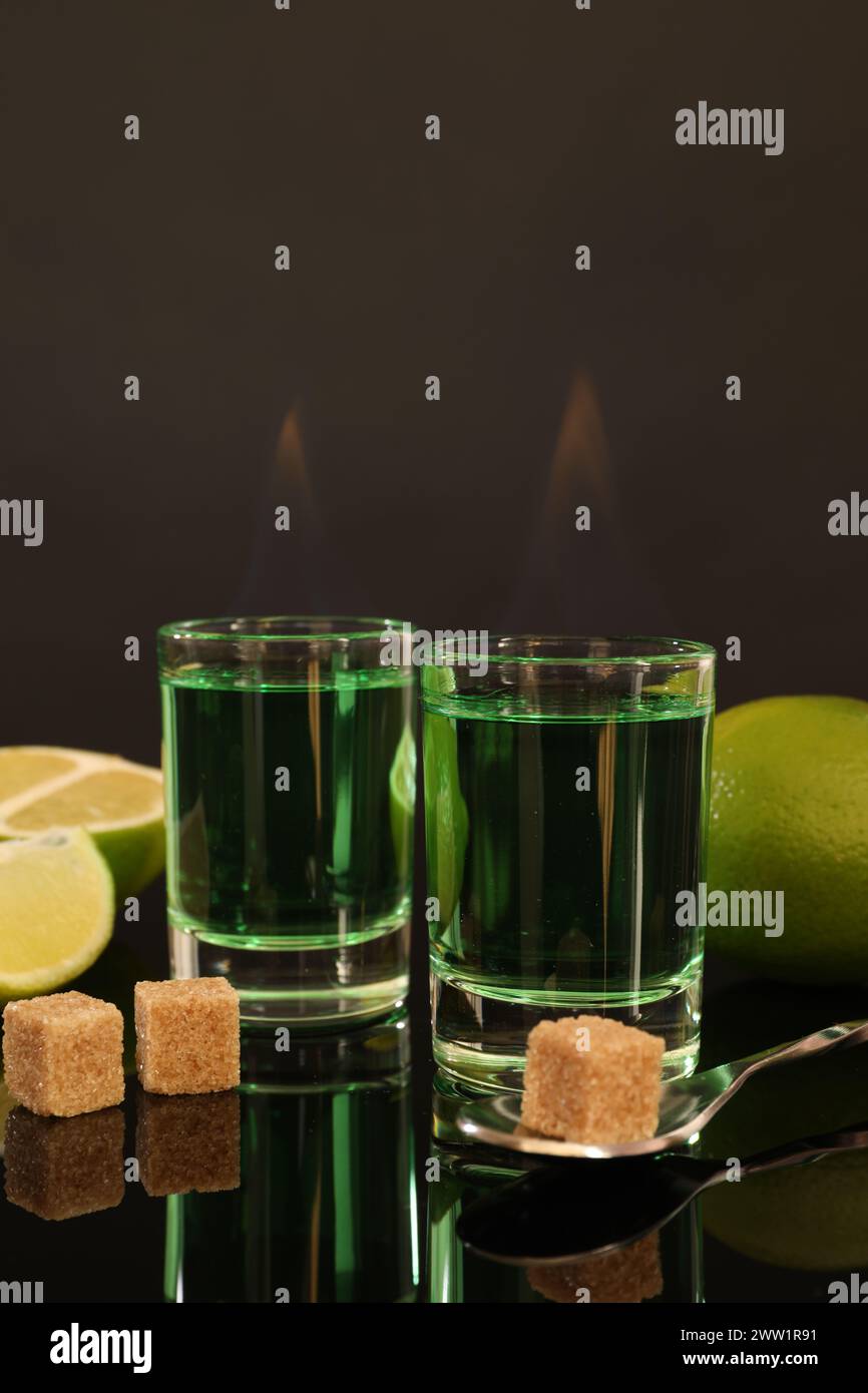 Flaming absinthe in shot glasses, brown sugar, lime and spoon on mirror ...