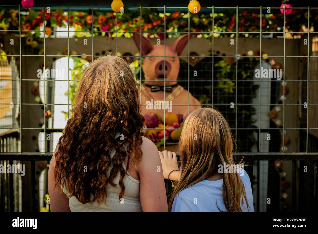 Two girls curiously observe a dressed-up pig amidst a colorful backdrop ...