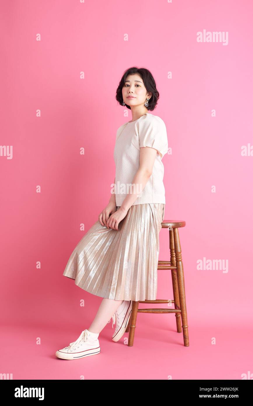 A woman in a white shirt and gold pleated skirt sitting on a stool ...