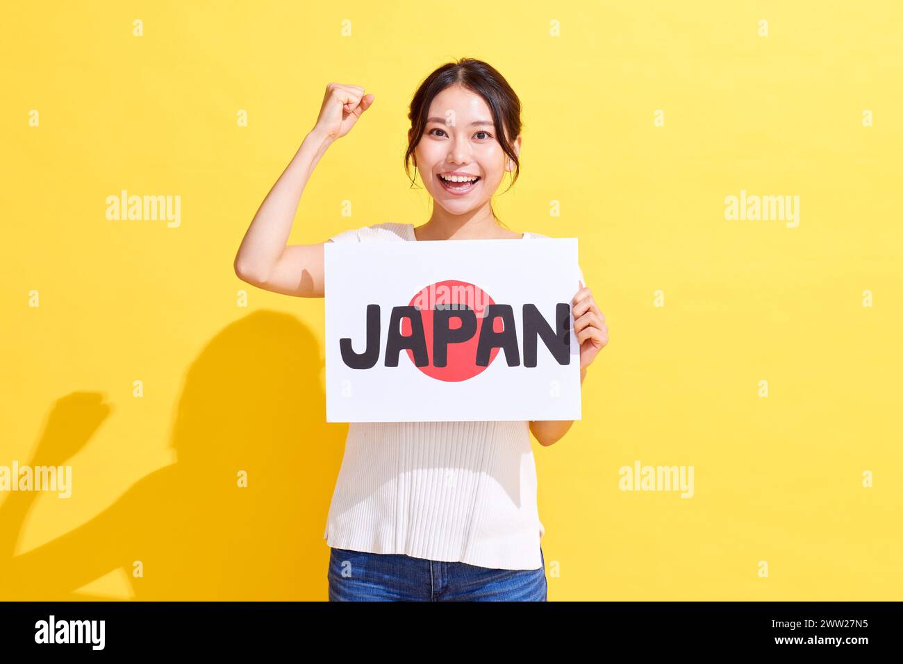 Japanese woman holding up sign with Japanese text on yellow background ...