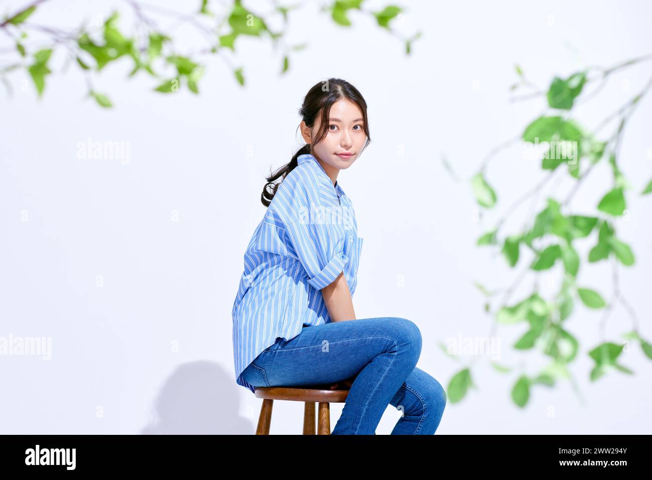 A woman sitting on a stool with a blue shirt and jeans Stock Photo - Alamy